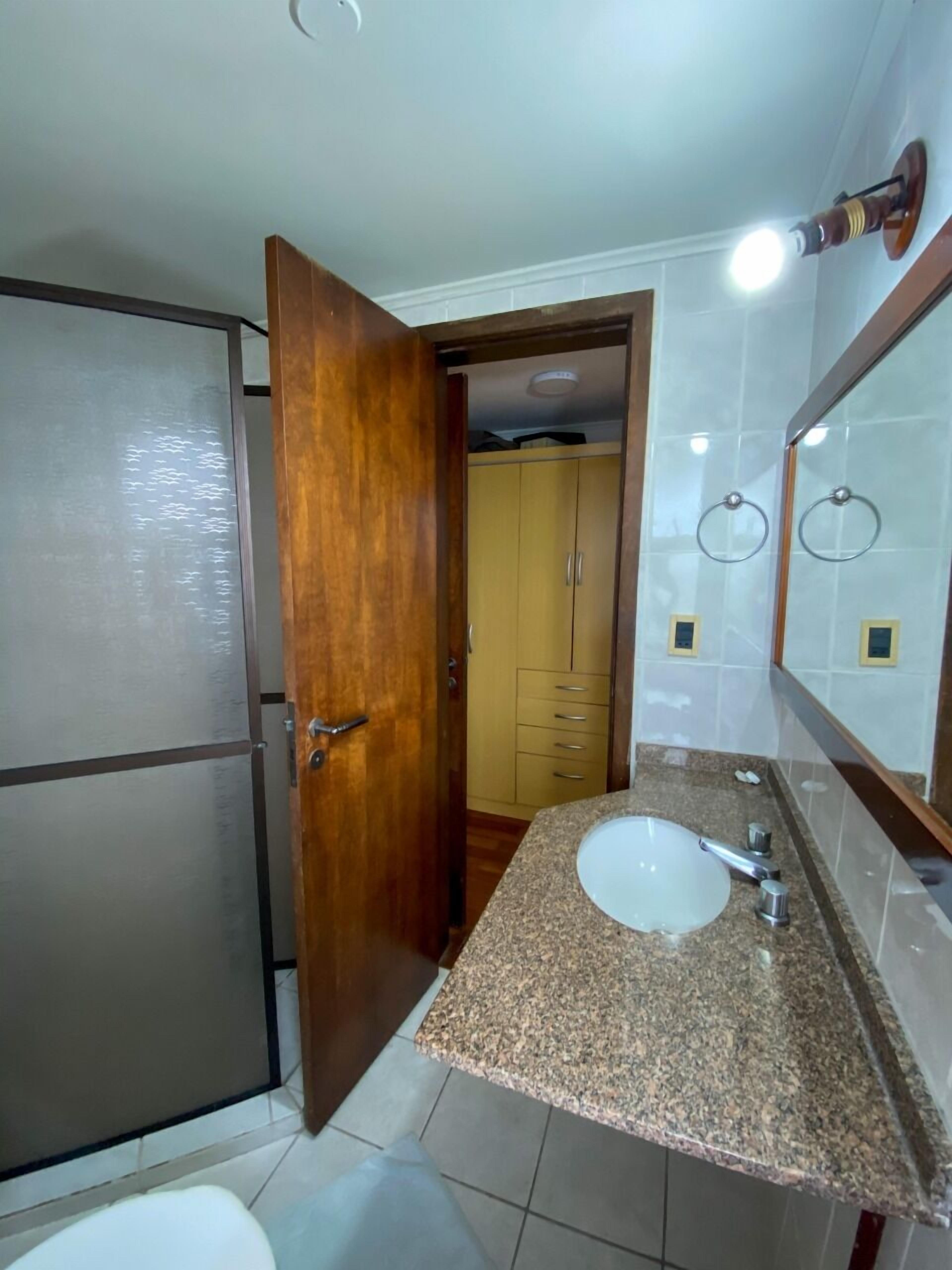 Casa de banho com lavatório de bancada em granito, porta de madeira e espelho.