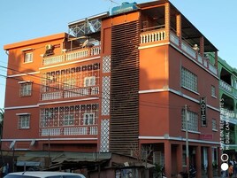 Um hotel de vários andares com varandas, uma placa indicando ser hotel, e uma entrada visível.