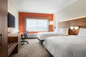 Quarto de hotel com duas camas, uma escrivaninha, uma cadeira, uma televisão e uma janela grande.