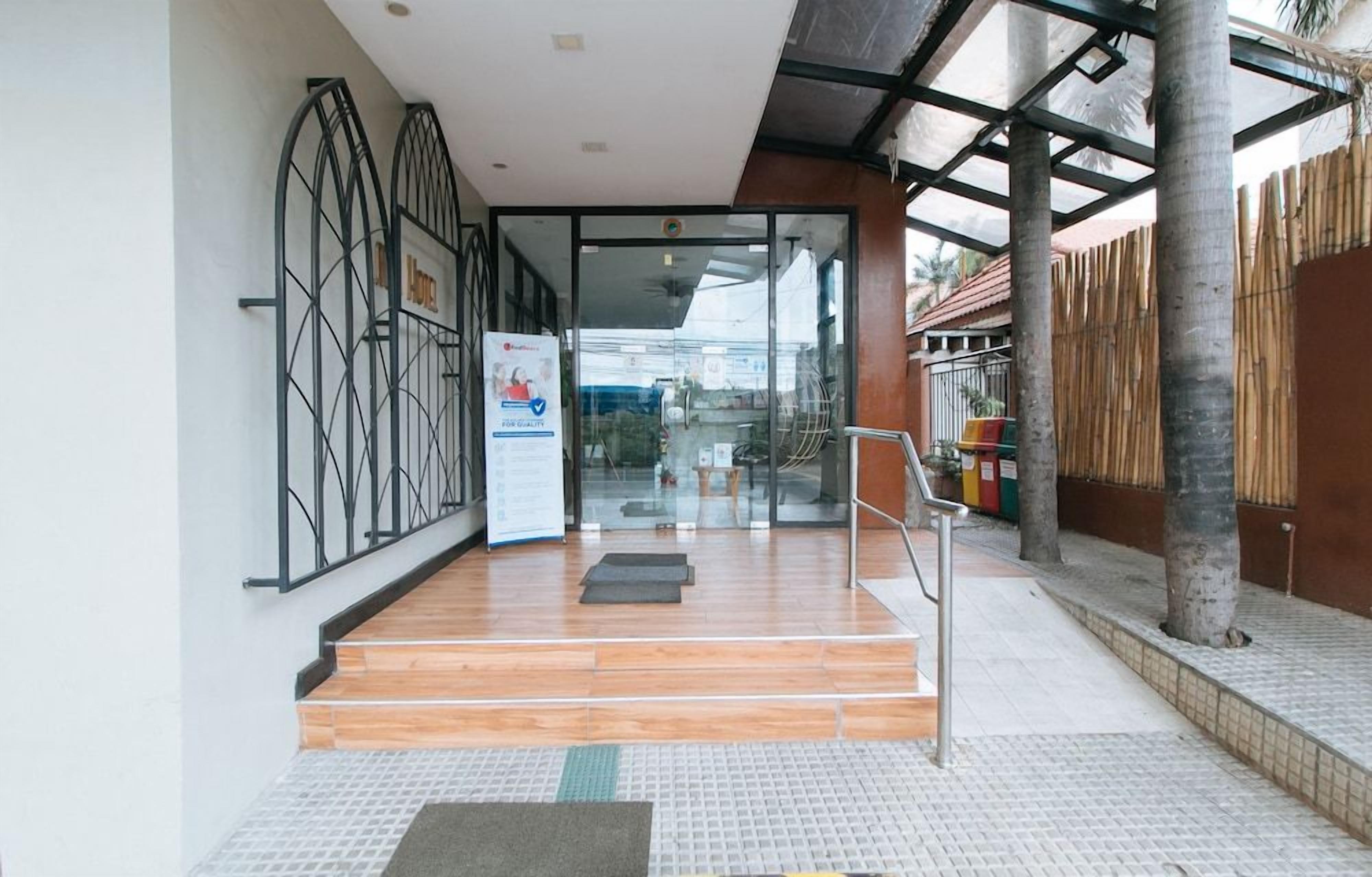 Entrada de hotel com escada de madeira, porta de vidro e cerca de bambu.