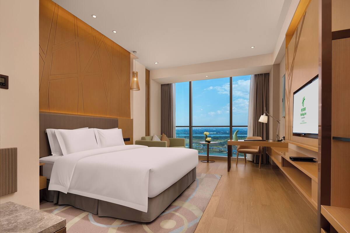 Quarto de hotel moderno com uma cama grande, uma mesa de trabalho e vista para o oceano.