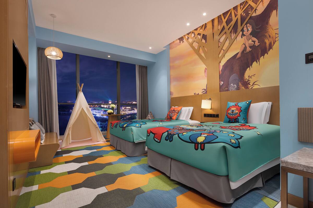 Quarto de hotel com duas camas, vista da cidade à noite, um mural grande e um tipi.