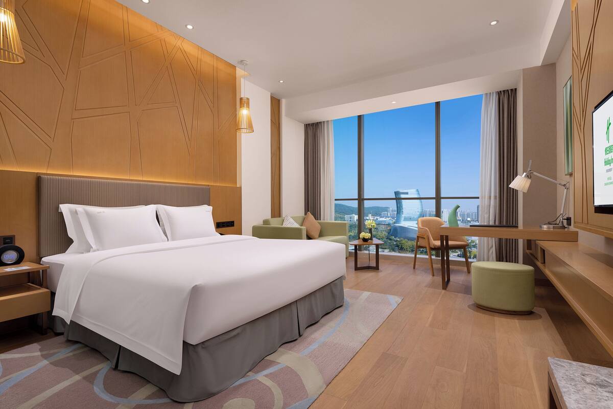 Quarto de hotel moderno com uma cama grande, uma escrivaninha e vista para a cidade.