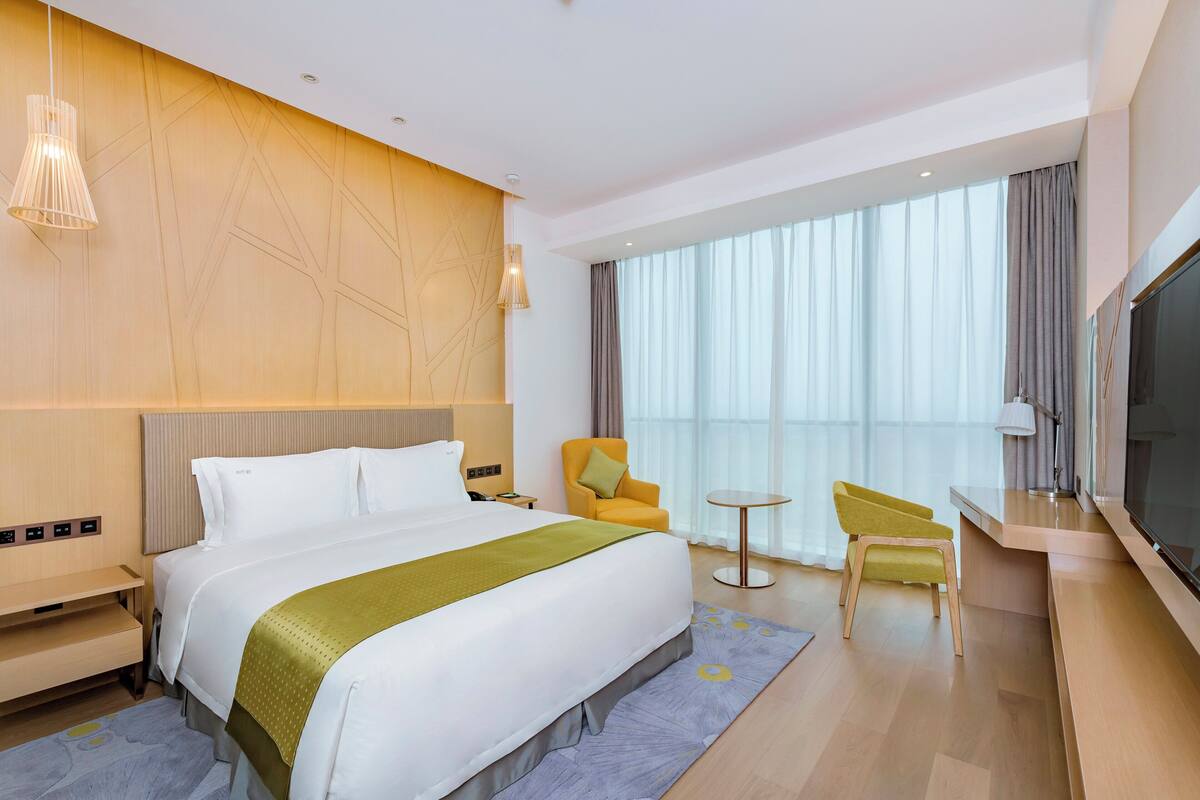 Quarto de hotel com uma cama grande, uma mesa com televisão, uma mesinha e uma cadeira.