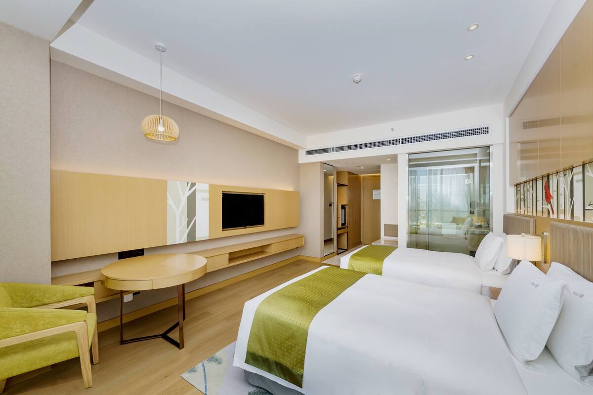 Quarto de hotel com cama, televisão, secretária e cadeira.