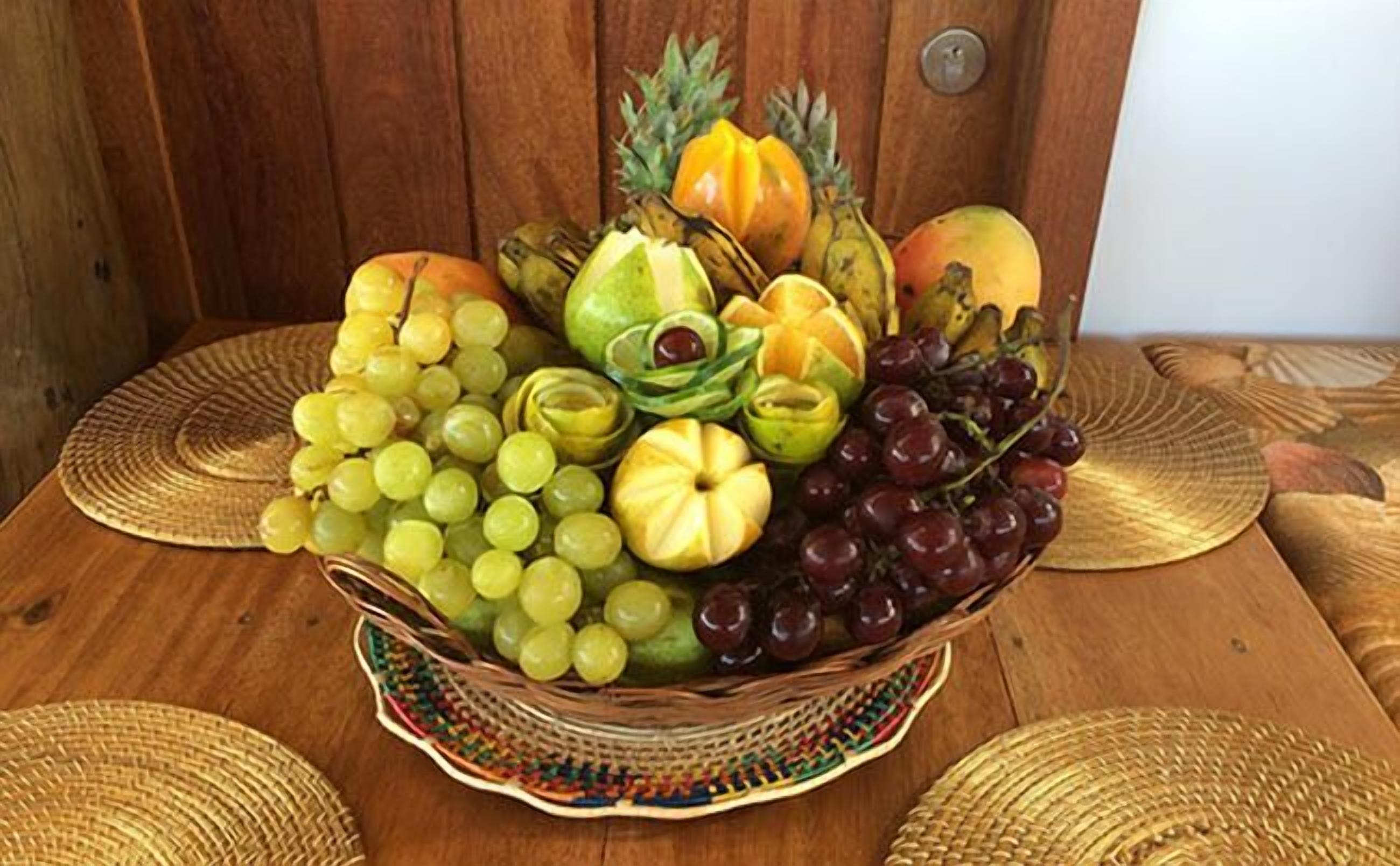 Uma cesta de frutas sobre uma mesa de madeira com jogos americanos trançados.