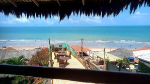 Vista da praia a partir de um alpendre coberto, com área de estar externa e vista para o oceano.