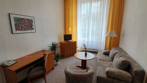 Uma sala de estar com uma escrivaninha de madeira, um sofá, uma mesinha e uma luminária.