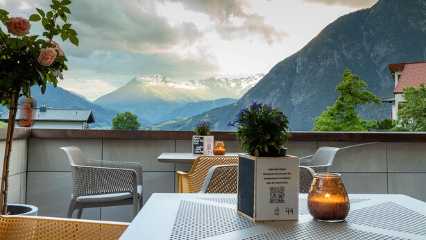 Um terraço com mesa, cadeiras, uma vela, um cardápio e vista para montanhas.