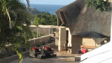 Um terraço no telhado com um telhado de palha, área de estar externa e vista para o oceano.