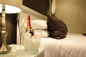 Uma cama com um travesseiro, uma garrafa de champanhe e uma taça de champanhe em um balde de gelo.