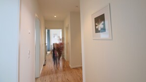 Um corredor com piso de madeira, paredes brancas e um quadro pendurado à direita.