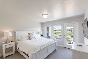 Quarto com cama, mesa de cabeceira, abajur e vista através de uma porta.