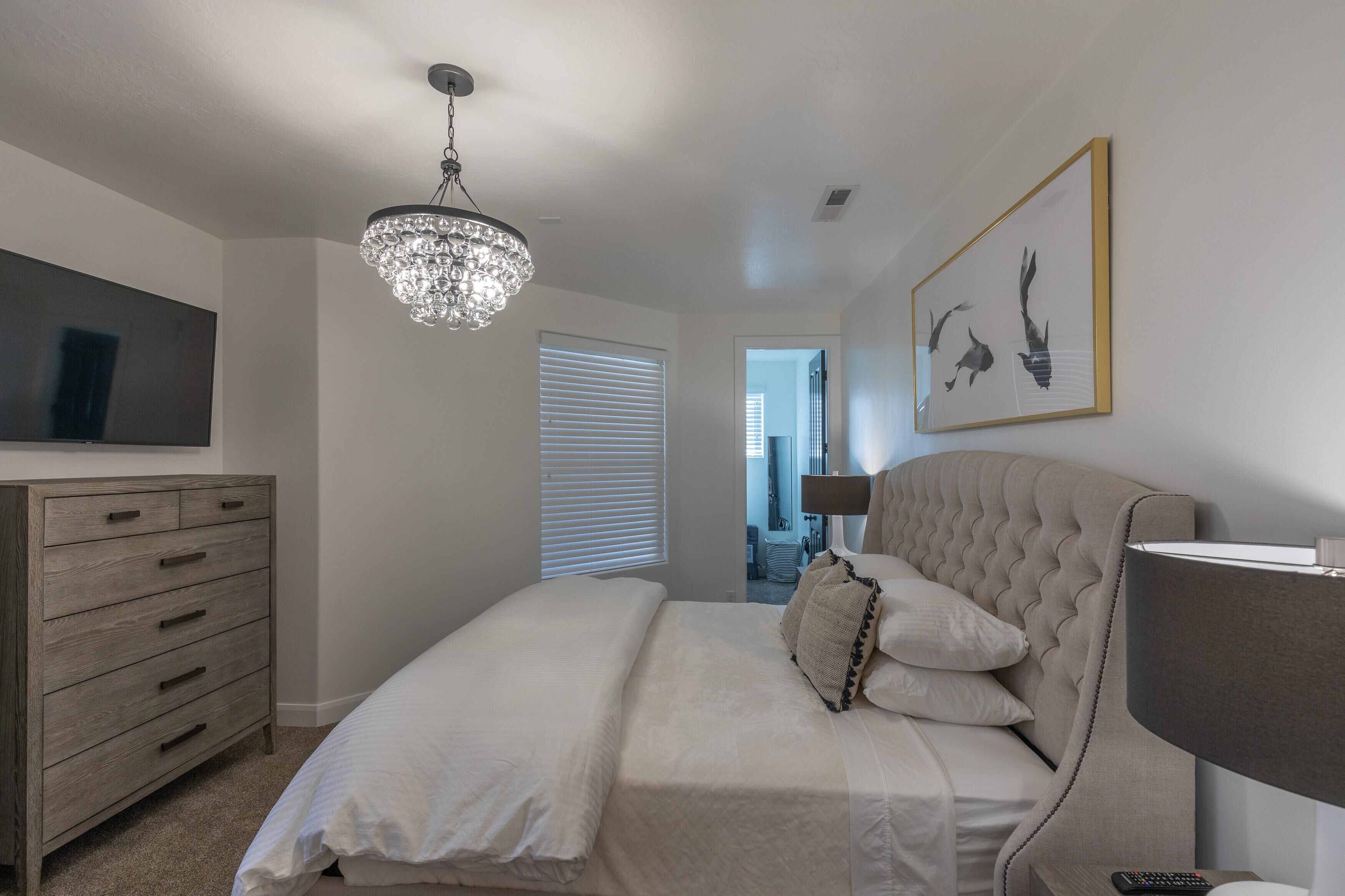 Quarto com cama, cômoda, lustre, obras de arte e televisão.