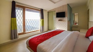 Quarto de hotel com uma cama grande, televisão presa na parede e uma janela com cortinas.