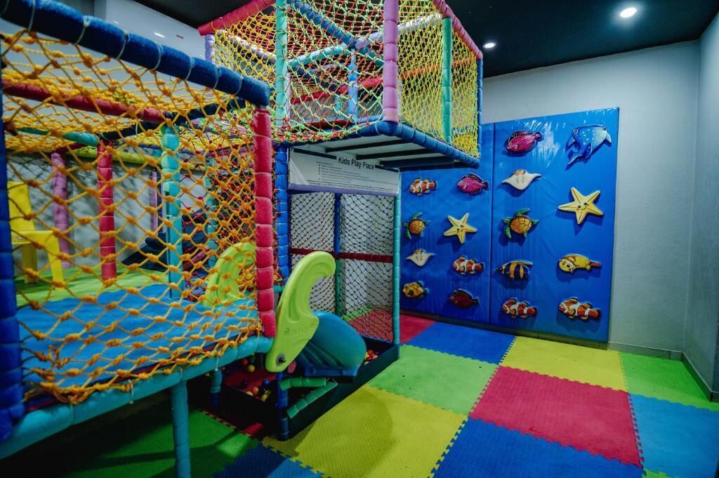 Espaço infantil com estrutura de escalada com rede, escorrega e painel decorado com peixes e estrelas-do-mar.
