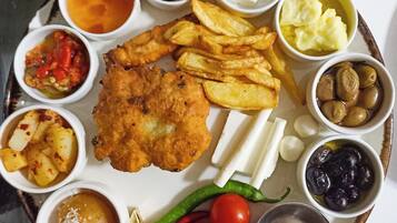 Um prato de peixe frito, batatas fritas e vários molhos, incluindo azeitonas e tomate.