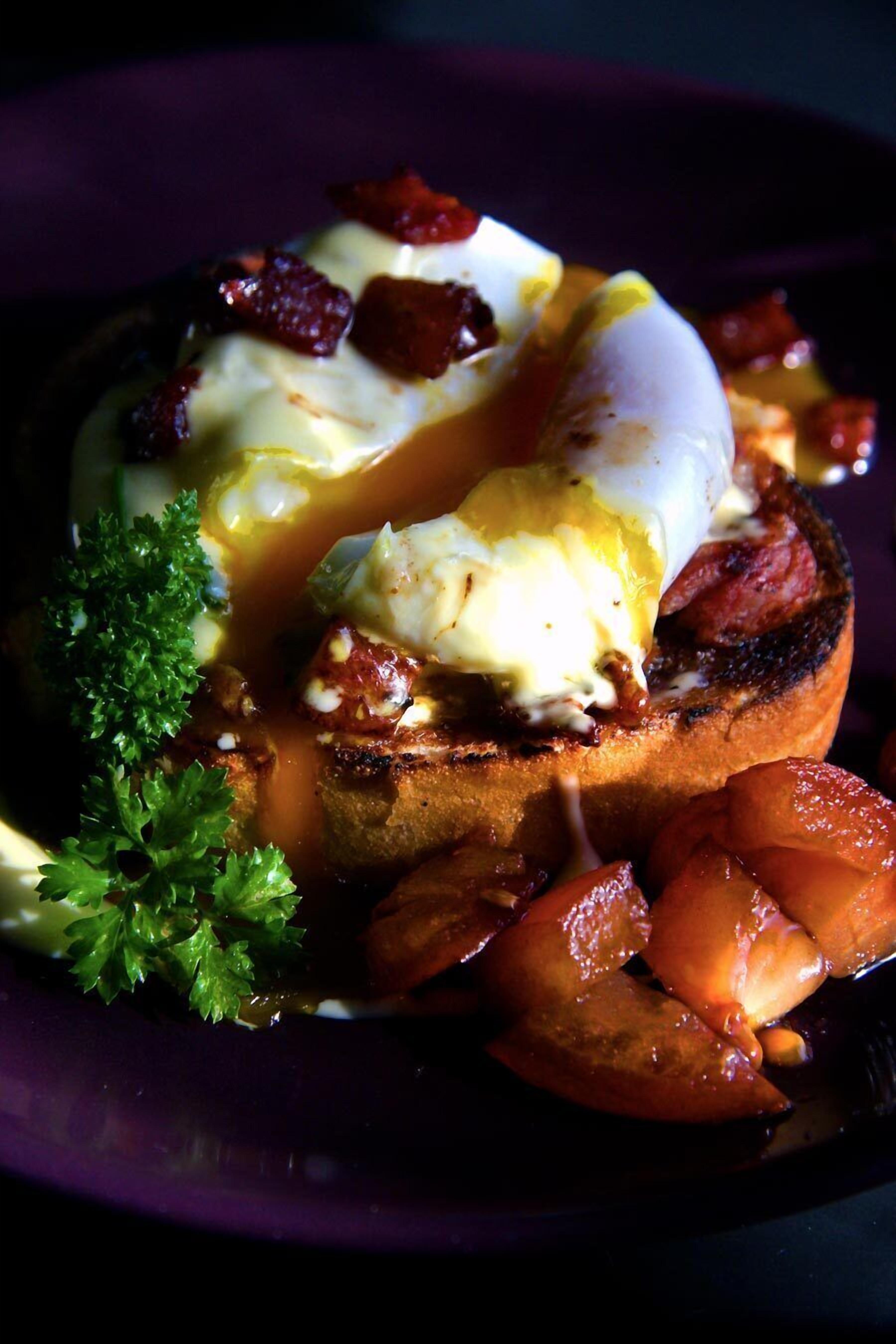 Prato de café da manhã com ovos pochê, bacon e tomate assado em torradas.