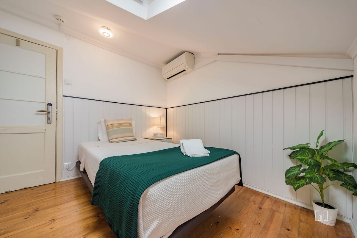Quarto com cama, mesa de cabeceira, abajur, ar condicionado e planta em vaso.