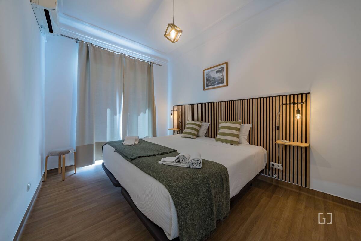 Um quarto moderno com uma cama grande, uma mesinha de cabeceira, uma cadeira, uma janela com cortinas, uma prateleira na parede e um quadro.
