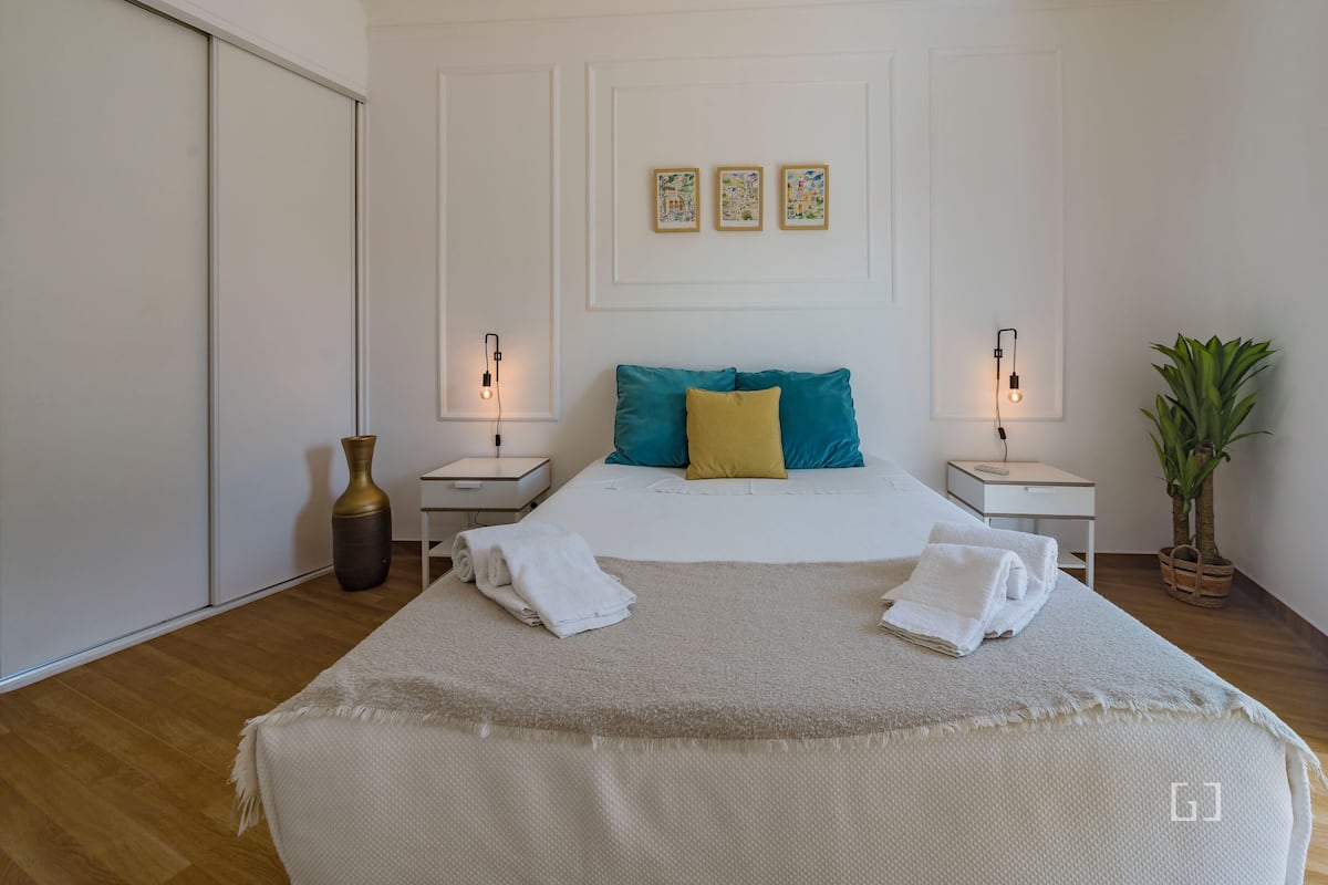 Quarto com uma cama grande, duas mesas de cabeceira, um criado-mudo, um vaso com planta e uma porta de correr.