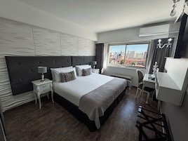 Quarto de hotel moderno com uma cama grande, uma escrivaninha, uma cadeira e vista da cidade pela janela.