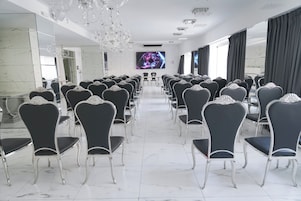 Uma sala de conferências com fileiras de cadeiras, uma tela grande e um candelabro.