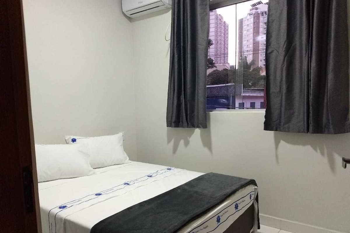 Quarto de hotel com cama, janela com cortinas e ar condicionado.
