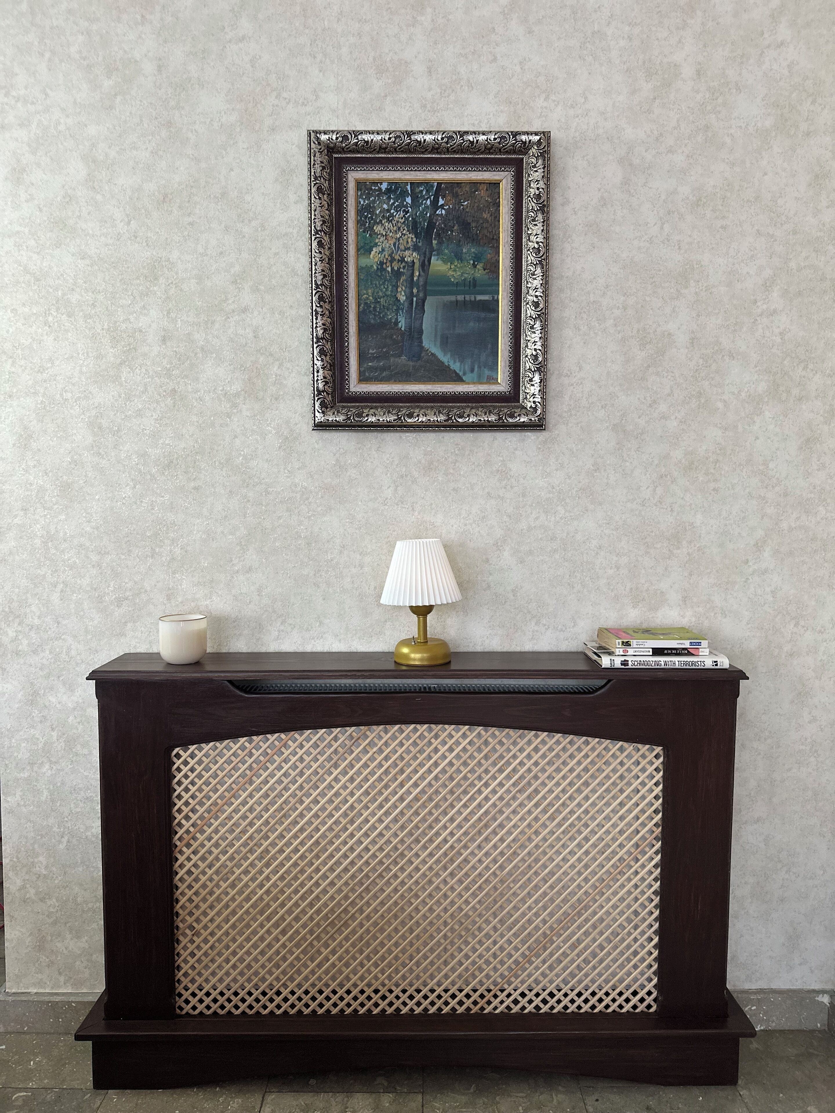 Um console de madeira escura com uma cesta trançada, uma caneca de cerâmica branca, um abajur dourado e um quadro na parede.