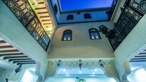 Visão do interior de um edifício com grades de ferro ornamentadas, uma coluna central e teto decorativo.