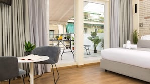 Quarto de hotel moderno com uma cama grande, uma mesa de jantar com cadeiras e uma varanda com plantas.
