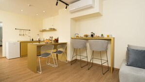 Um espaço de estar compacto com cozinha compacta, área de jantar com dois banquinhos e um sofá.