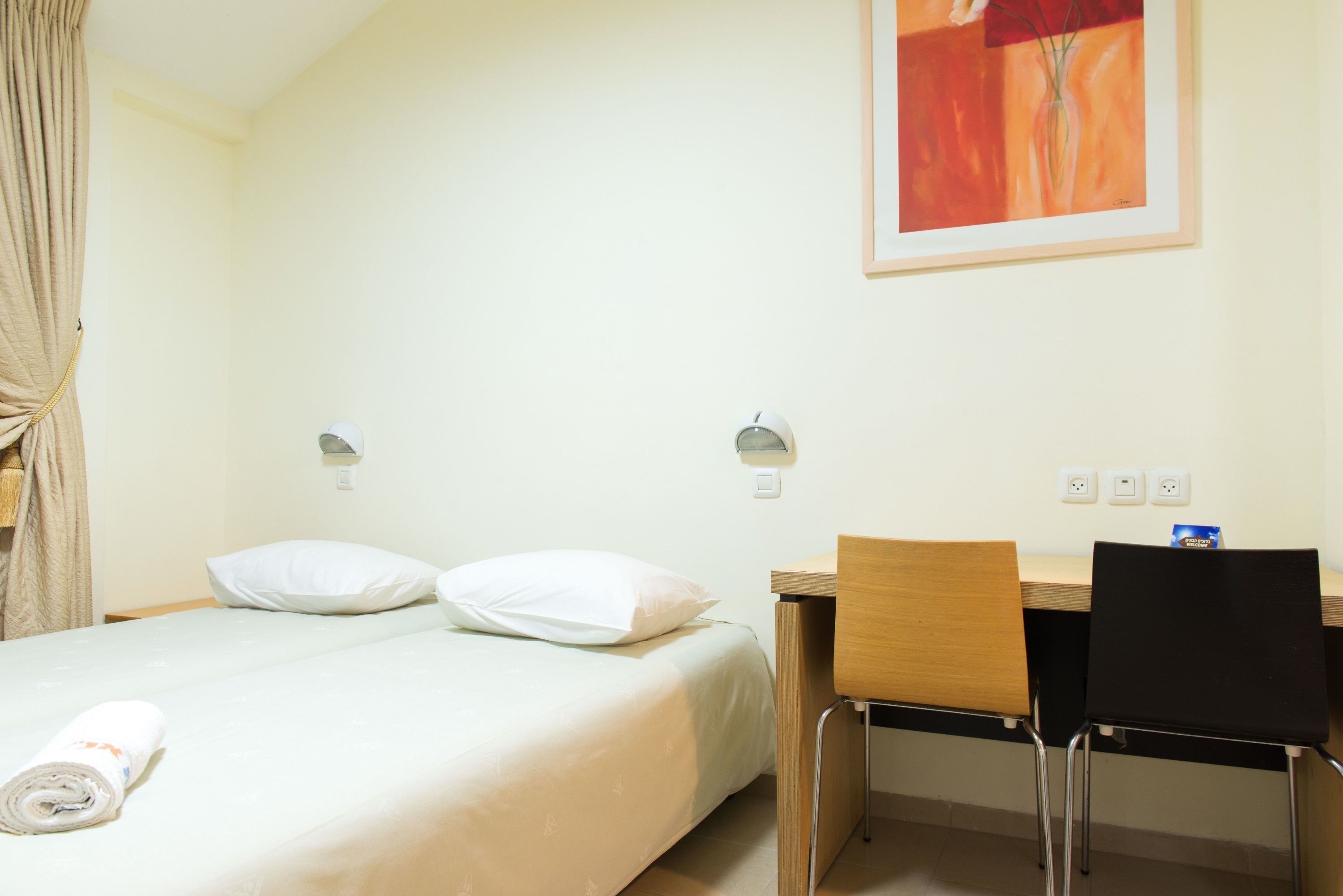 Quarto de hotel com uma cama, duas mesas de cabeceira, uma escrivaninha com cadeira e um quadro na parede.