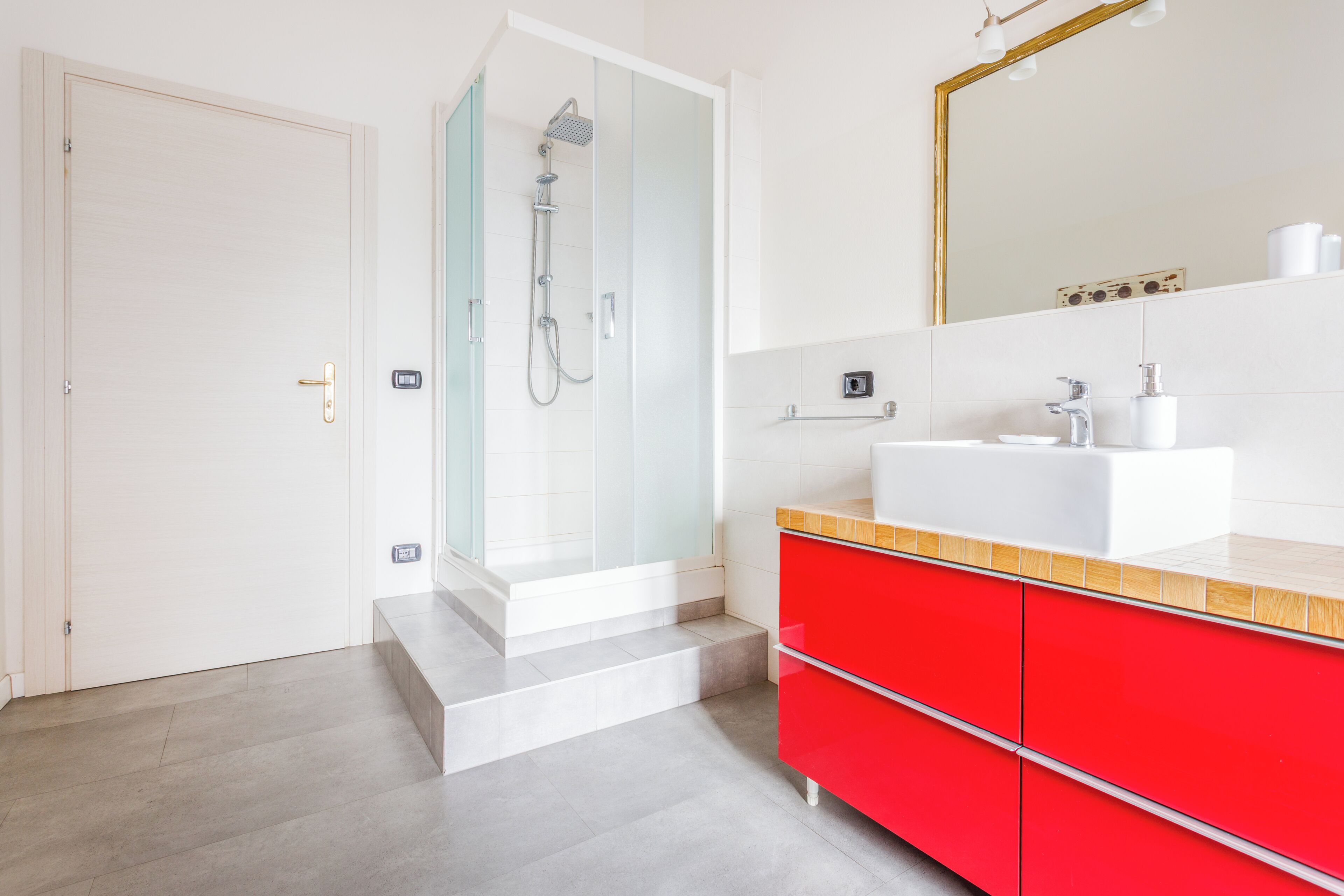 Uma casa de banho moderna com chuveiro, lavatório e toucador vermelho.