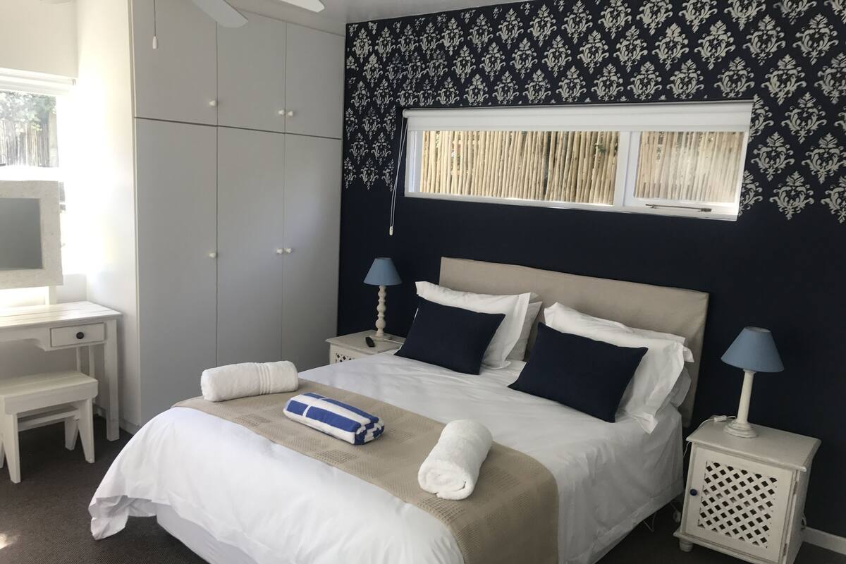 Quarto de hotel bem arrumado com uma cama grande, mesas de cabeceira com luminárias, um guarda-roupa e uma janela com vista.