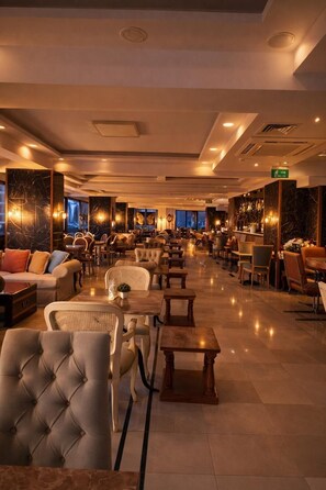 Um amplo hall de hotel com áreas de estar, um bar e vista para a paisagem urbana.