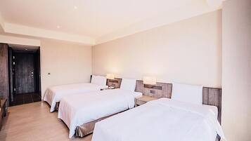 Quarto de hotel com três camas de solteiro, piso de madeira e porta que dá para um corredor.