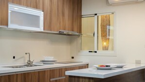 Cozinha moderna com armários de madeira, bancada branca, micro-ondas e janela com cortina decorativa.