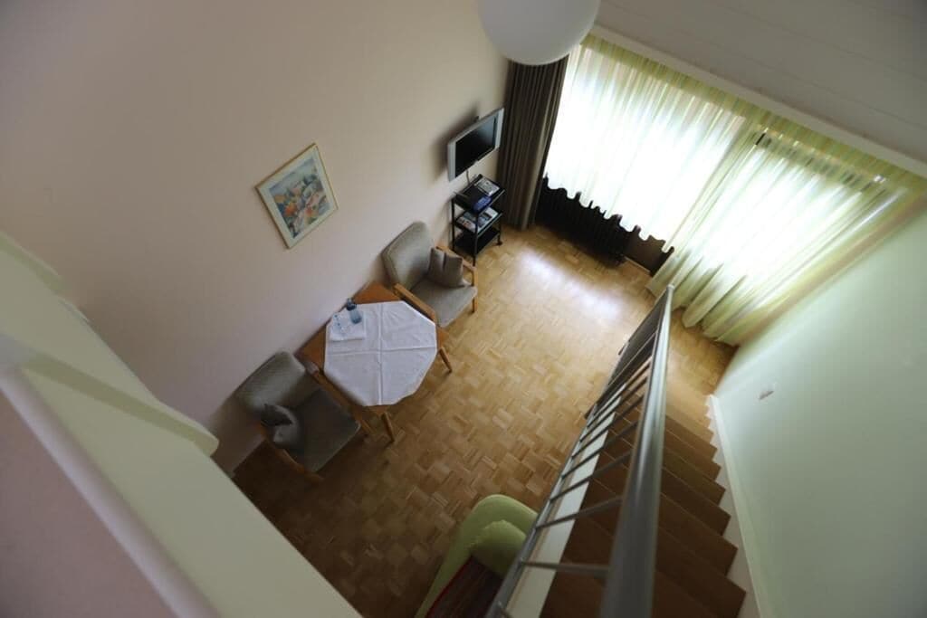 Um quarto com escada, uma pequena mesa com cadeiras, uma televisão e uma janela com cortinas.