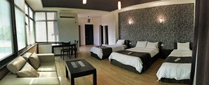 Quarto de hotel moderno com três camas, um sofá, uma mesa pequena e uma escrivaninha.