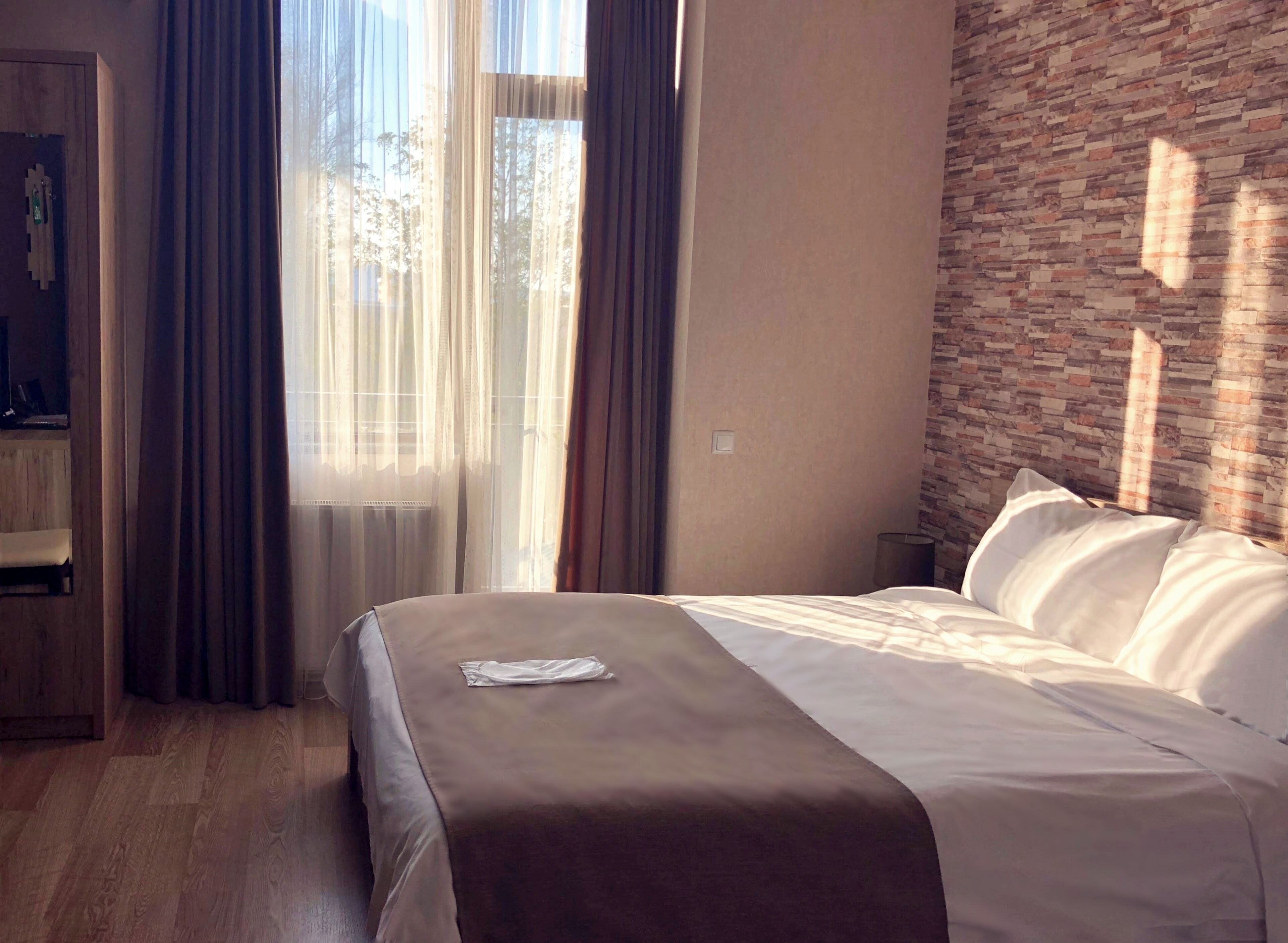 Quarto de hotel com uma cama grande, piso de madeira, parede de tijolos e uma janela com cortinas.