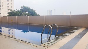Piscina no terraço com escadas de metal, rodeada por um muro baixo e um deck revestido com azulejos.