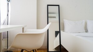 Quarto moderno e minimalista com uma escrivaninha branca, uma cadeira branca, cama com roupa de cama branca e um espelho grande na parede.