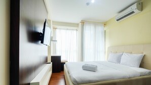 Quarto de hotel com cama, televisão na parede, ar condicionado e janela com cortinas.