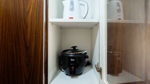 Uma cozinha compacta com um cozido lento preto na bancada, uma chaleira branca numa prateleira e uma máquina de café noutra prateleira.