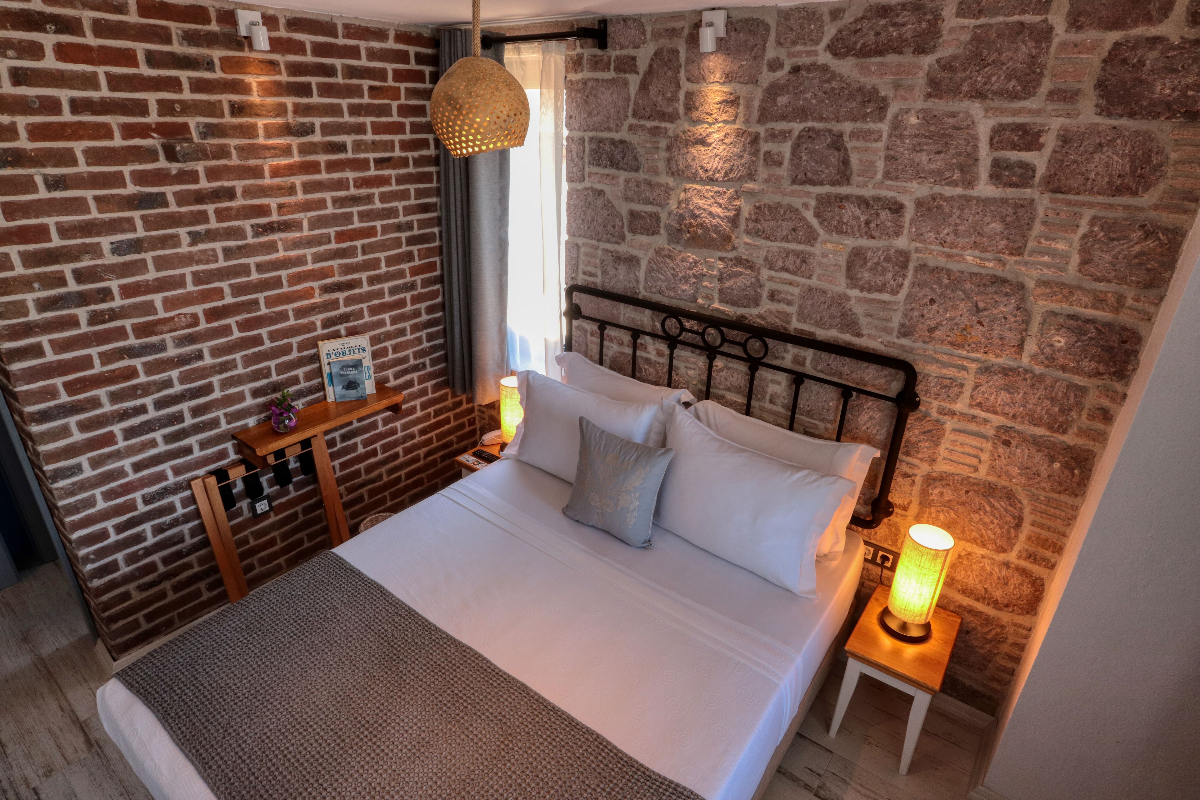 Quarto com parede de tijolos, cama com roupa de cama branca, mesa de cabeceira de madeira e aquecedor fixado na parede.