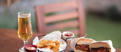 Uma refeição com sanduíche, batatas fritas e um copo de cerveja sobre uma mesa de madeira.