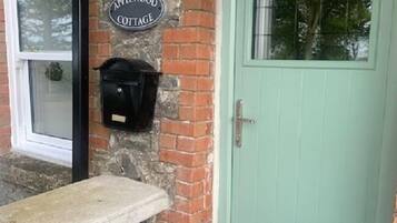 Entrada de um chalé com muro de pedra, porta verde e placa com a inscrição 'Applewood Cottage'.