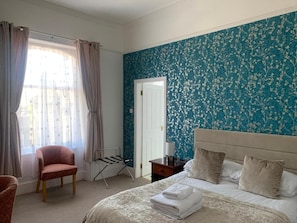 Quarto de hotel com cama, cadeira, mesa de cabeceira e janela com cortinas.