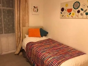 Quarto com cama, janela com cortinas, parede com pintura floral e pequena imagem de uma maçã.